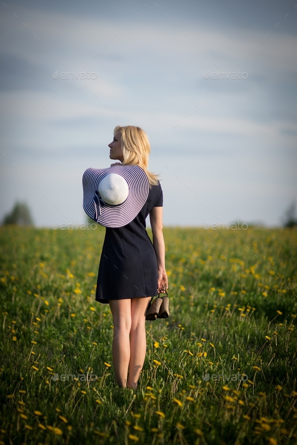 Slim young woman walking barefoot in a blossoming dandelion meadow ...