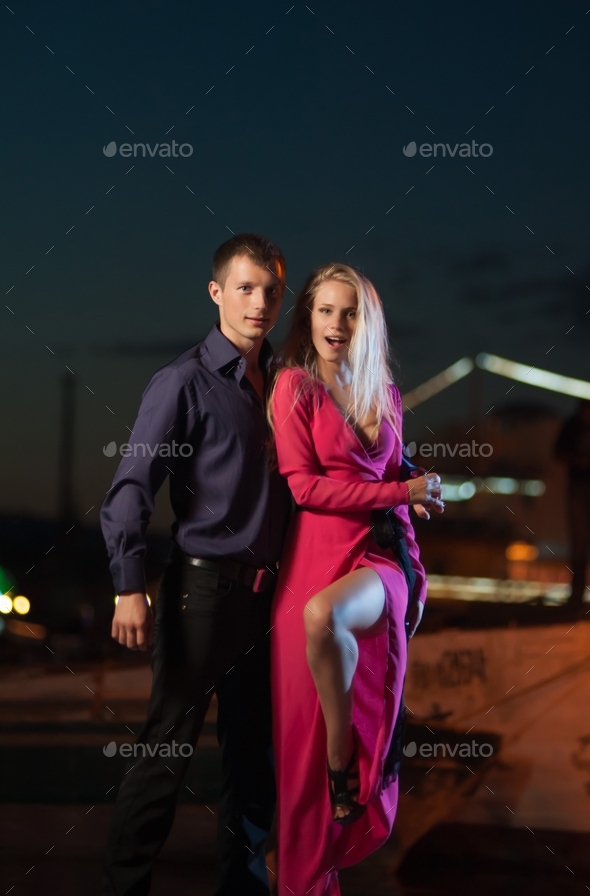 Young guy with a girl hug and dance tango at night on the city street ...