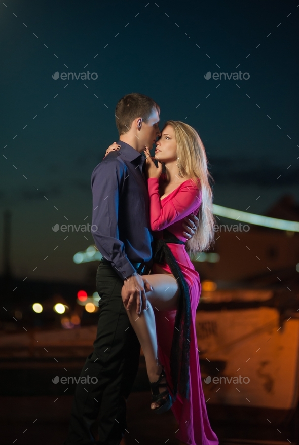 Young guy with a girl hug and dance tango at night on the city street ...
