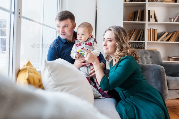 A young family with a little son sits at home by the window and looks ...