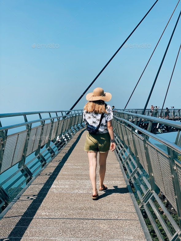 Rear view of woman walking over suspension bridge Stock Photo by David ...