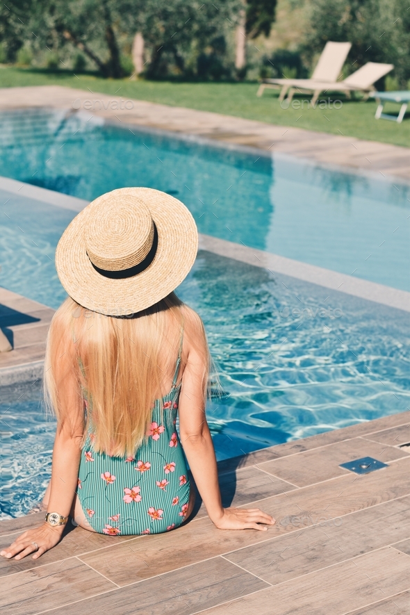 Rear view of woman in bathing suit sitting at the poolside Stock Photo ...