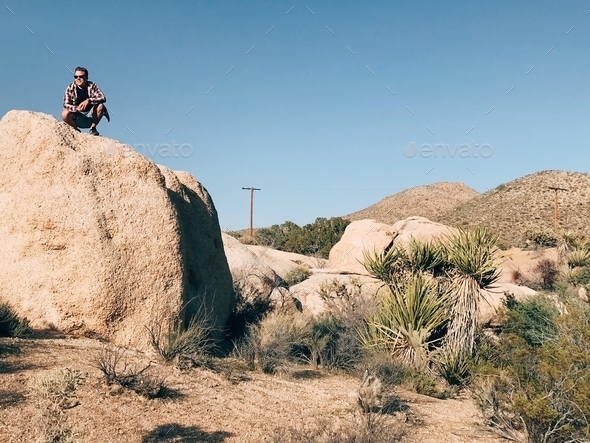 Man sitting on big rock in Mojave desert Stock Photo by David_Tanke