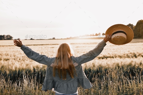 Rear view of woman with raised arms in front of field at sunset Stock ...