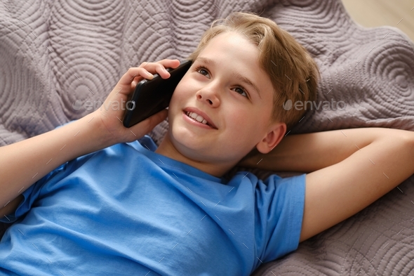 Generation Z boy talking on the phone while lying on his bed at home ...