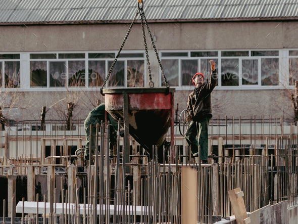 Workers at the construction site fix the cargo with cement with slings ...