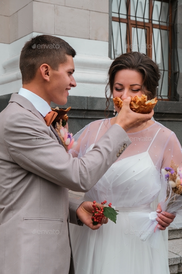 Happy young bride feeding wedding cake to groom outdoors. Weeding ...