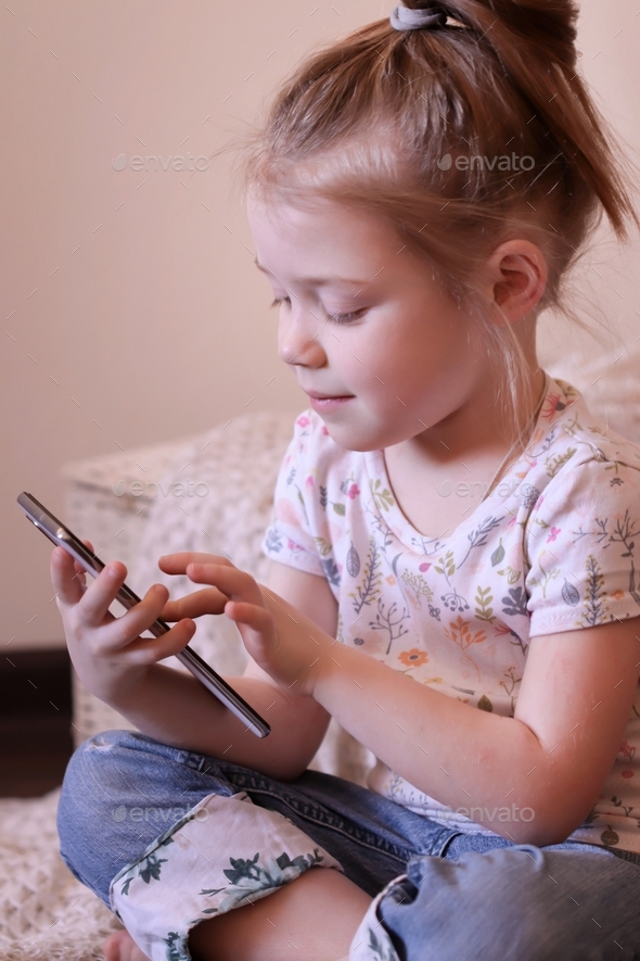 A cute little girl uses the phone, browses social networks, searches ...