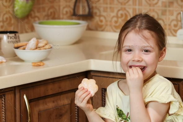 Little cute girl holding a cookie she took from a plate on the kitchen ...