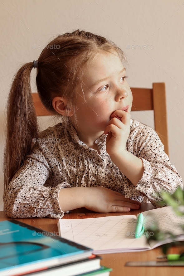 A cute girl sits at the table and writes letters in a notebook ...