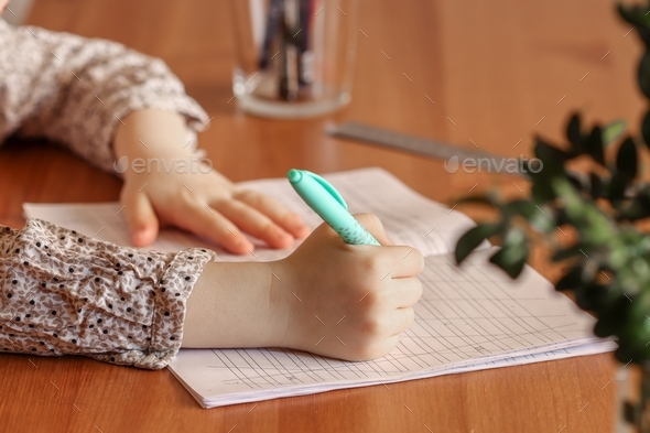 A cute girl sits at the table and writes letters in a notebook ...