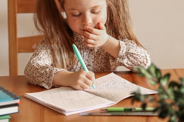 A cute girl sits at the table and writes letters in a notebook ...