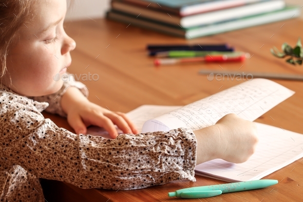 A cute girl sits at the table and writes letters in a notebook ...