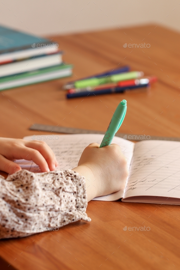 A cute girl sits at the table and writes letters in a notebook ...