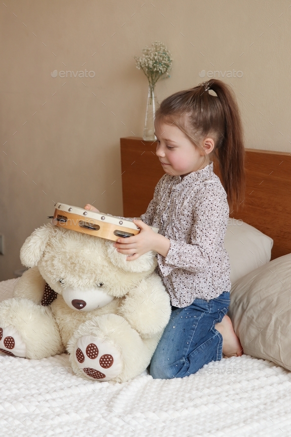 The girl plays with a teddy bear and musical instruments, depicts a ...