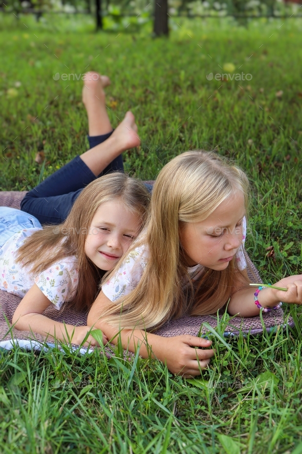 Two cute sisters lie on the grass hugging each other and share secrets. candid family Stock ...