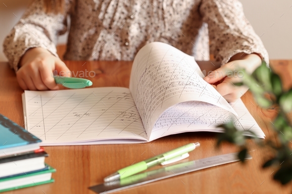 A cute girl sits at the table and writes letters in a notebook ...