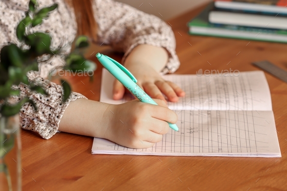 A cute girl sits at the table and writes letters in a notebook ...