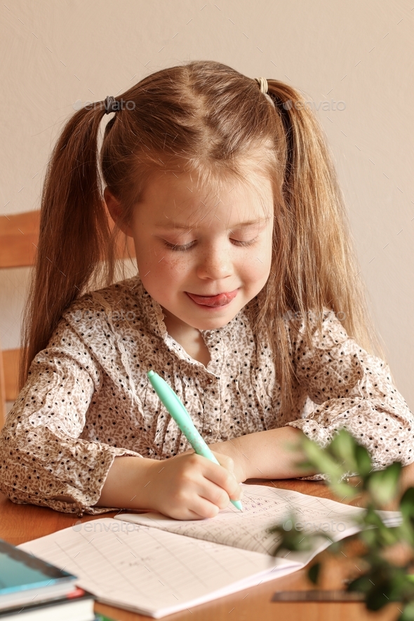 A cute girl sits at the table and writes letters in a notebook ...