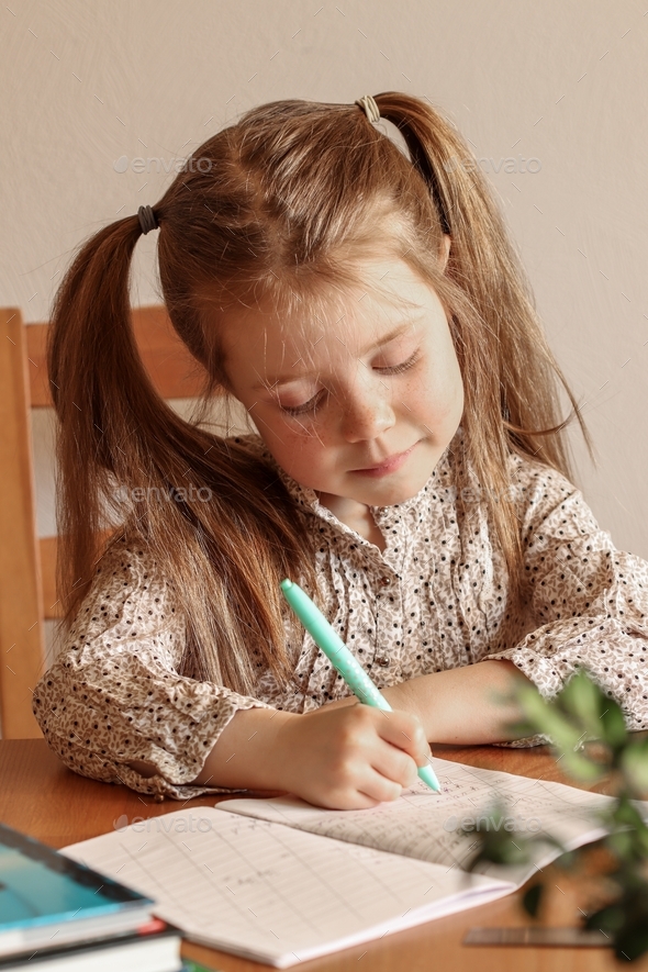 A cute girl sits at the table and writes letters in a notebook ...