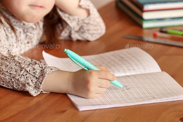 A cute girl sits at the table and writes letters in a notebook ...