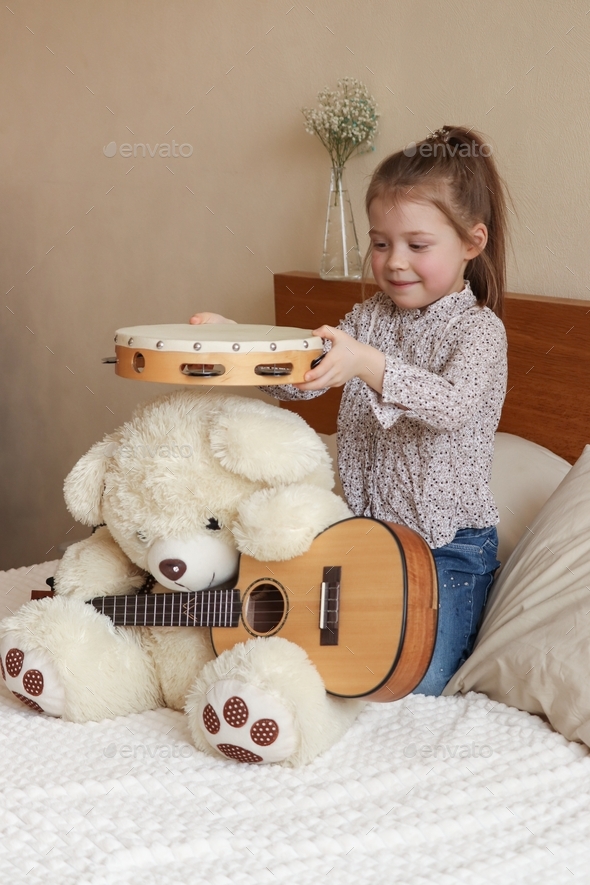 The girl plays with a teddy bear and musical instruments, depicts a ...