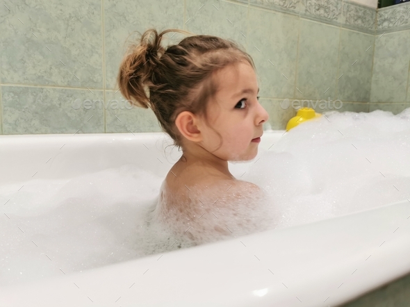 Cute little girl take a bath with foam and toys. People from behind ...
