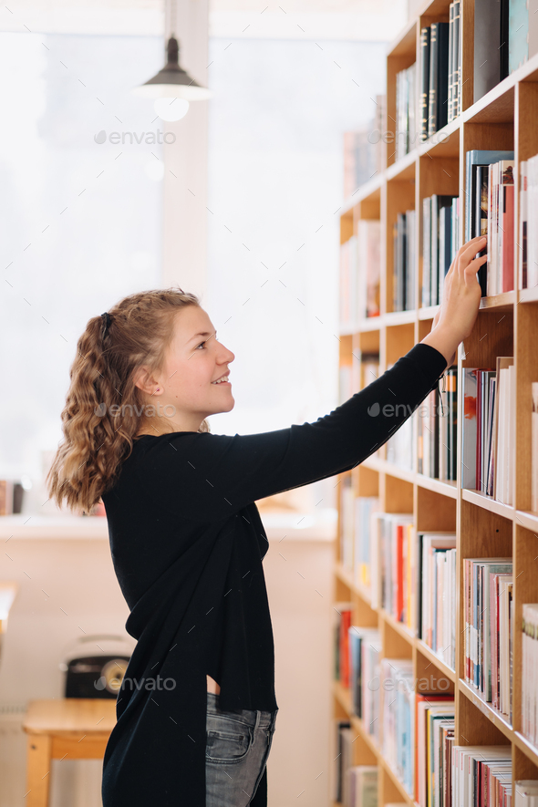 Teenager girl picking a book on a library shelf Stock Photo by arthurhidden
