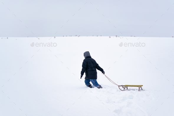 A person walks through deep snowdrifts in felt boots, dragging an empty ...