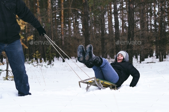 In the forest, a man sleds a young happy woman who laughs and is about ...