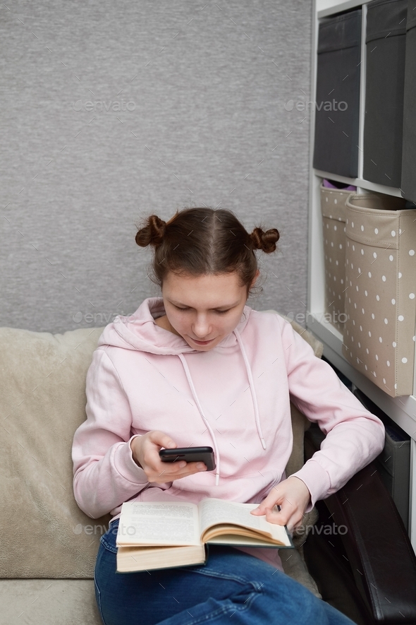 At home a young woman sits on the couch reading a book being distracted ...
