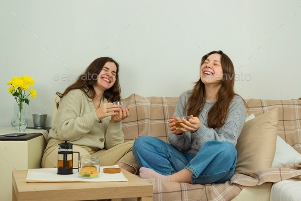 Two young women laughing hard drinking tea while sitting on the couch ...