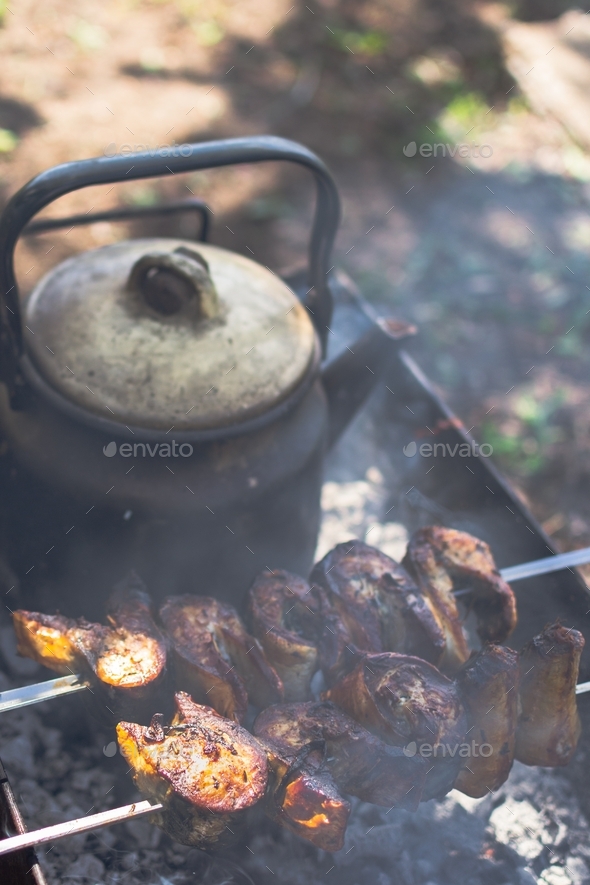 Top view of a fish baked on a grill on hot coals and an old kettle ...