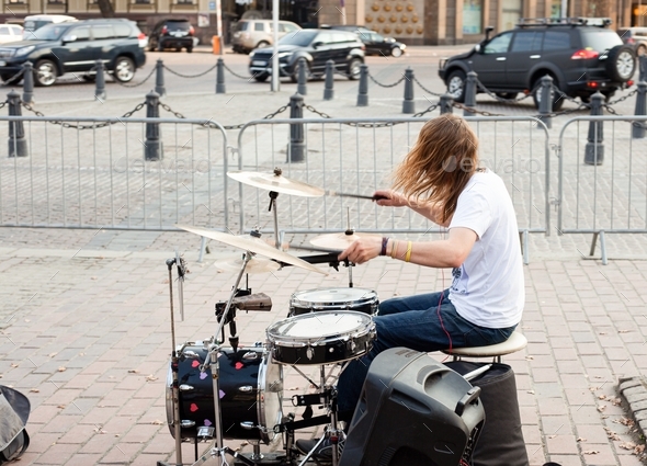 A street musician plays the drums on the street. Drum set. Long haired ...