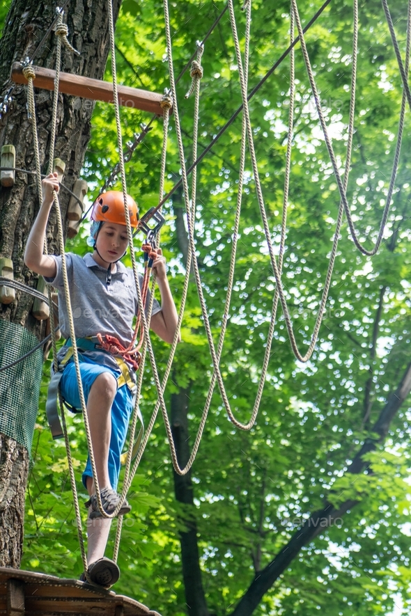 Rope park. A boy in a helmet walks on suspended rope ladders ...