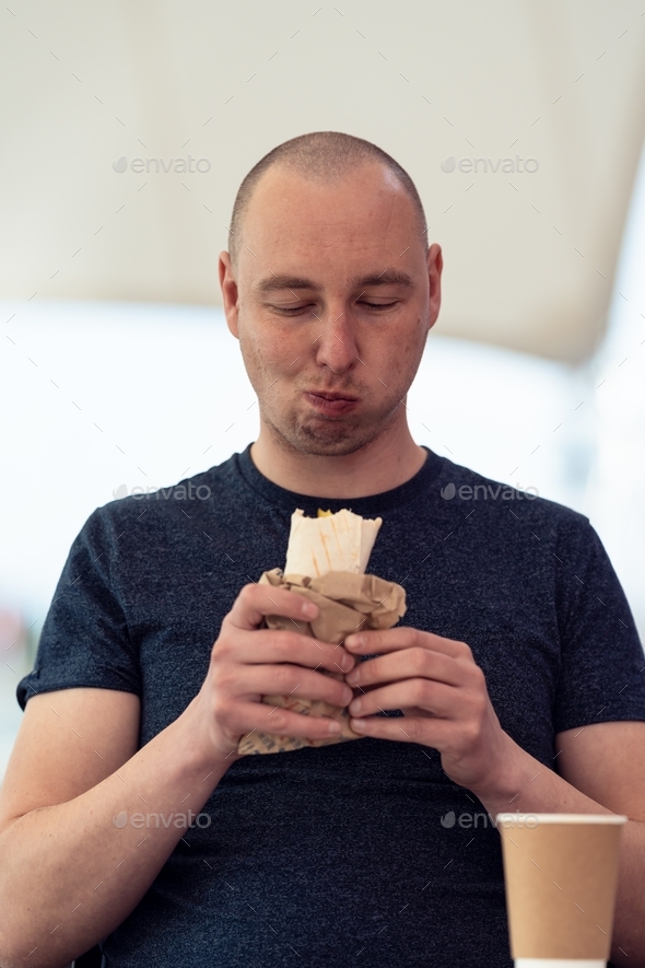 White man eating tasty shawarma with appetite. Eco cup of tea or coffee ...