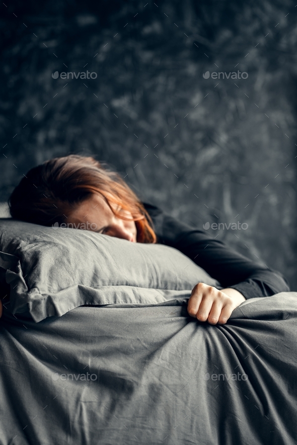 Young woman lying on bed in depression. Hand clenching sheet with pain ...