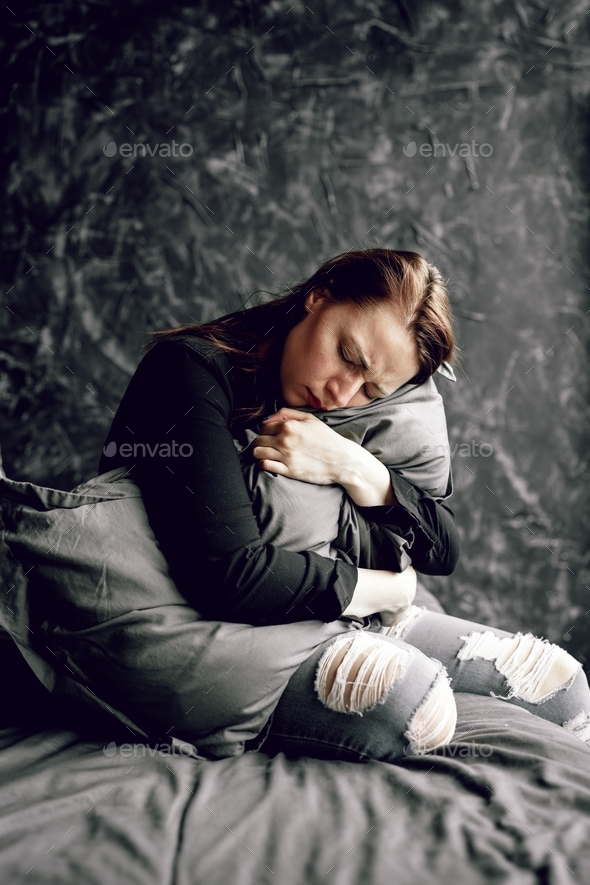 Young depressed woman sitting on bed and hugging pillow. Feeling sad ...