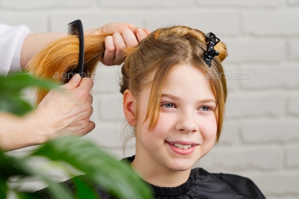 Hairdresser making a hair to cute girl in hair salon. Young girl at ...