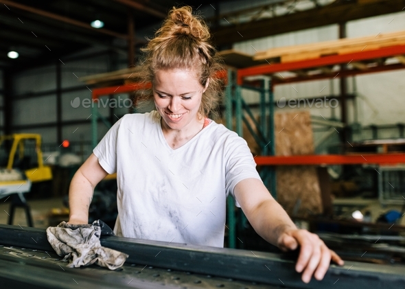 A female maker smiling while she cleans steel with a rag in a workshop ...