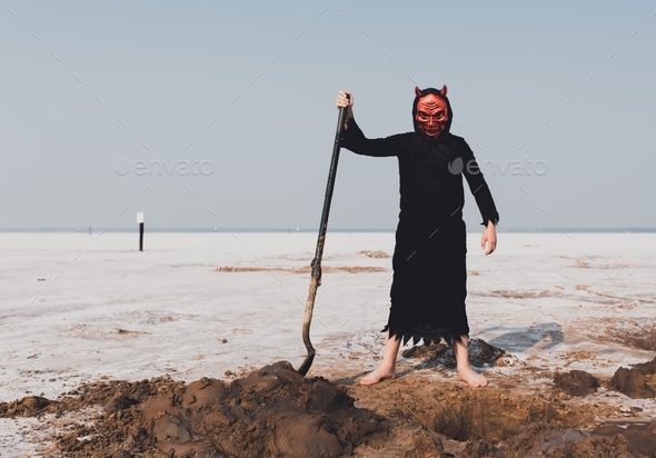 A boy wearing a scary devil costume and holding a shovel at the salt ...