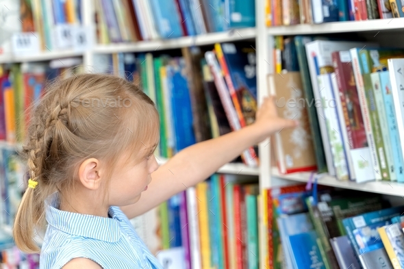 Little girl chooses, takes book with fairy tales from shelf in children ...