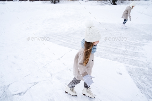 Beautiful little cute girl learn to skate on ice skating rink in park ...