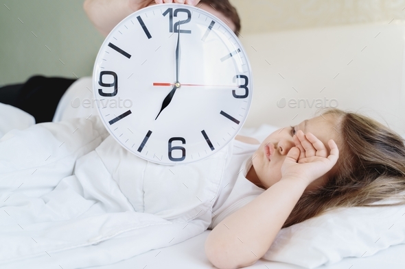 Dad wakes up little sleeping in bed girl,daughter. Big alarm clock ...