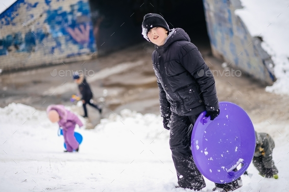 chick carries an ice sled to slide down a snow-covered slide in winter ...