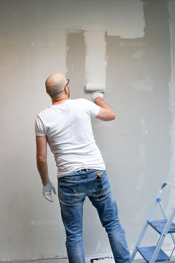 Full length of a man painting the wall in white. New home. Home ...
