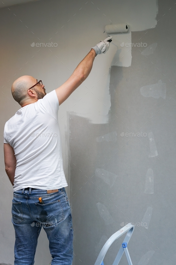 Full length of a man painting the wall in white. New home. Home ...