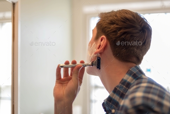Clean cut young man shaving in the bathroom getting ready for work ...
