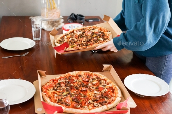 Two big pizzas has been delivered and woman serving them on the table ...