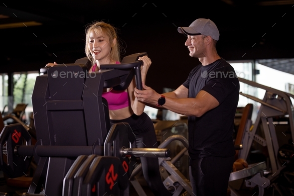 A trainer helps a young woman use exercise tools in the gym. Stock ...